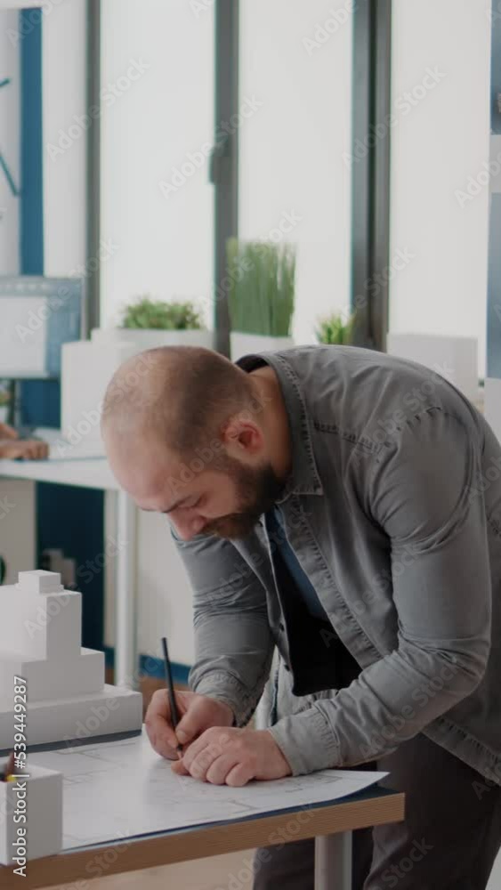 Vertical video: Man architect taking notes on blueprints plan to design ...