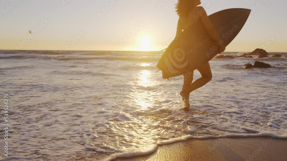 The young female surfer walks on the beach with a surfboard in her hand ...