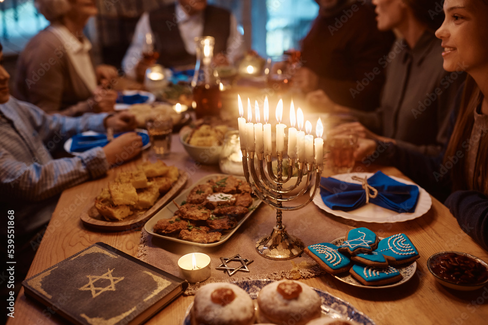 Lit candles in menorah on dining table with extended Jewish family in ...