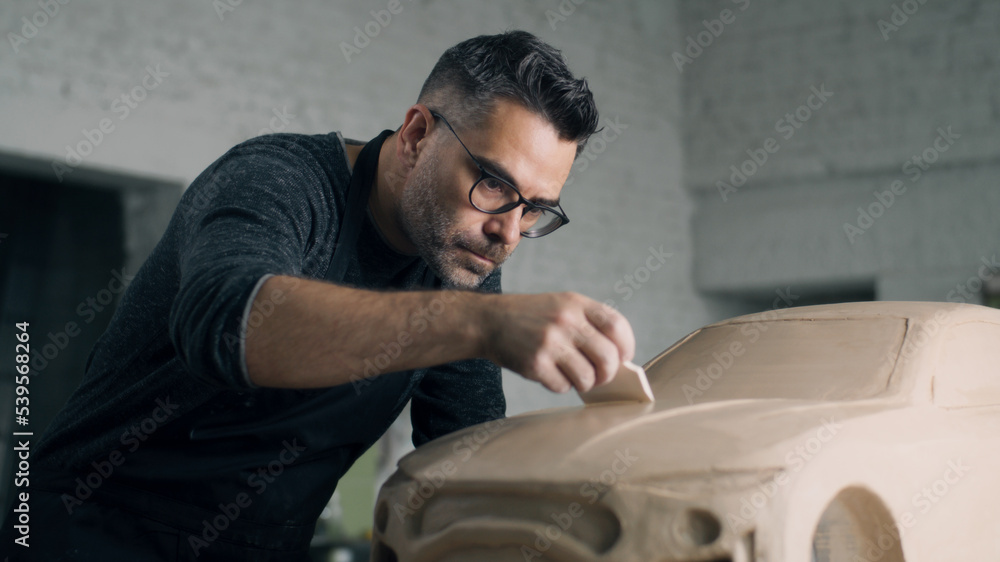 Experienced automotive designer with an apron works on the clay ...