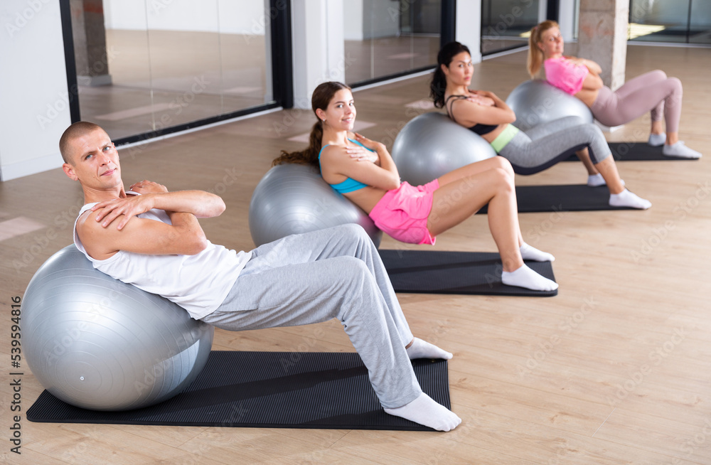 Four people doing back crunches on swiss balls during pilates training ...