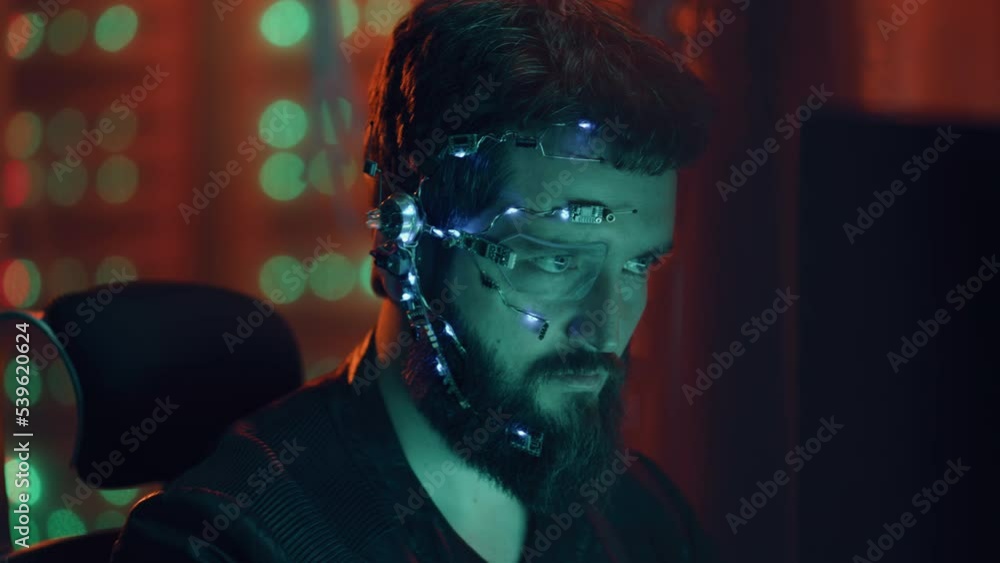 Brunette guy works on the computer with neon lights in background ...