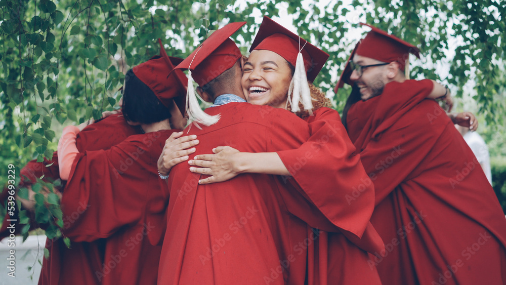 Joyful friends graduating students in gowns and mortarboards are ...