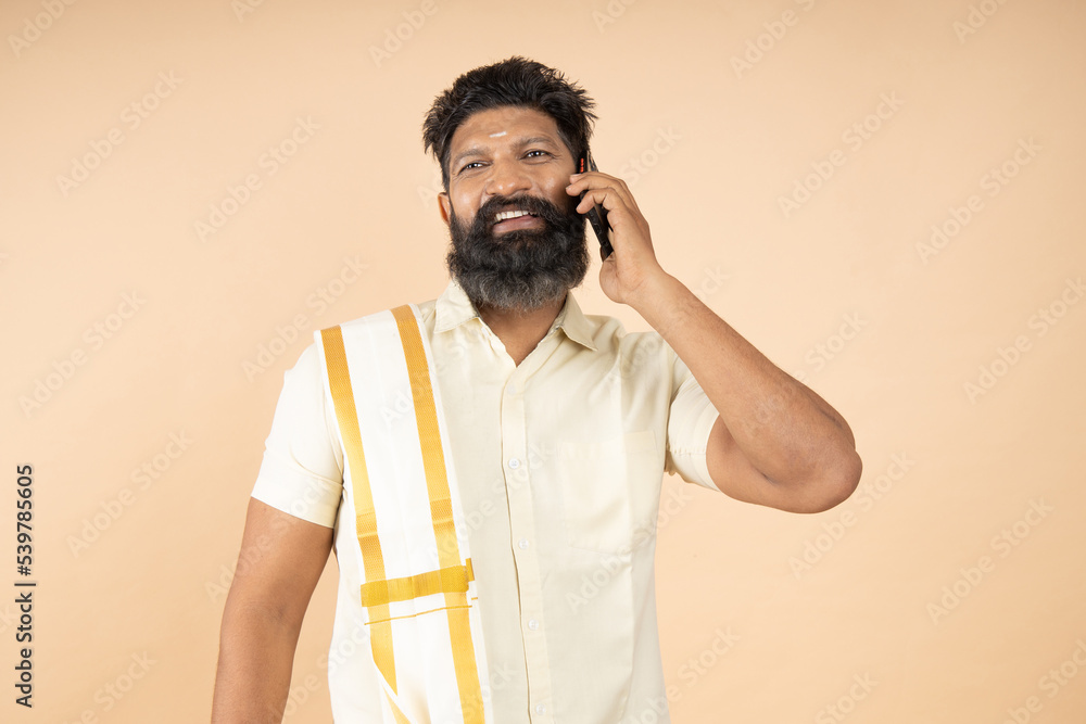 Happy South indian beard man talking on mobile phone isolated on beige ...