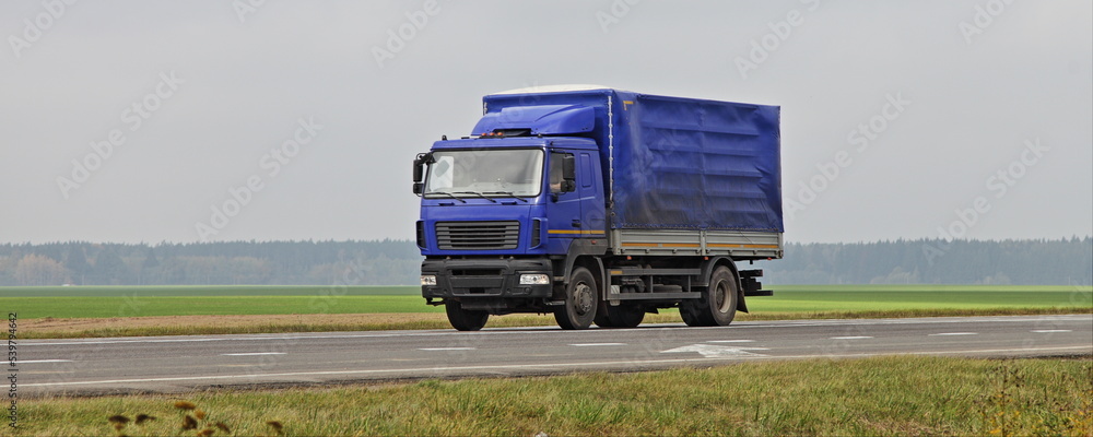 Blue tented truck drive on countryside highway road on green field ...