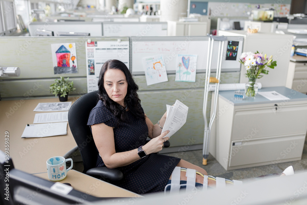 Businesswoman with broken leg in brace working at computer with feet up ...