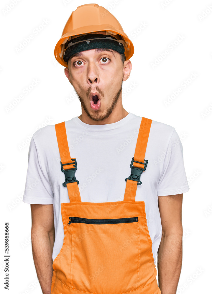 Hispanic young man wearing handyman uniform and safety hardhat scared ...