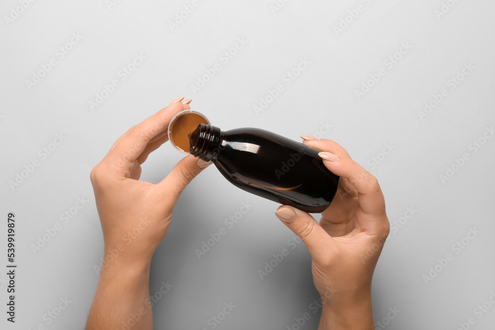 Woman pouring cough syrup from bottle into cup on light background ...