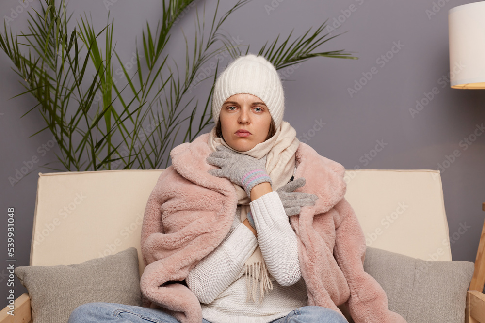 Indoor shot of sad upset woman in cold room sitting on the sofa wearing ...