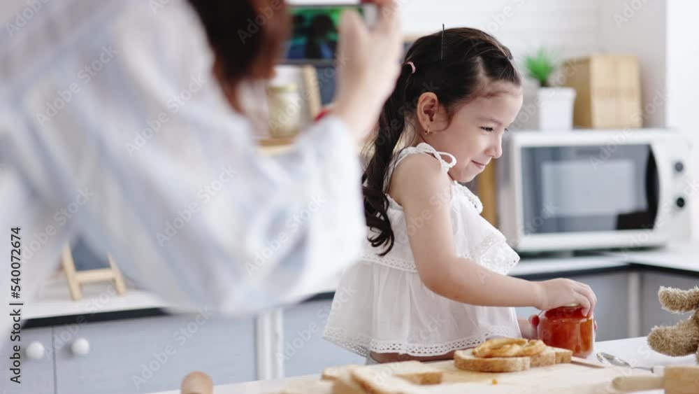 toddler girl is learning to cook bread in the kitchen with her mom with ...