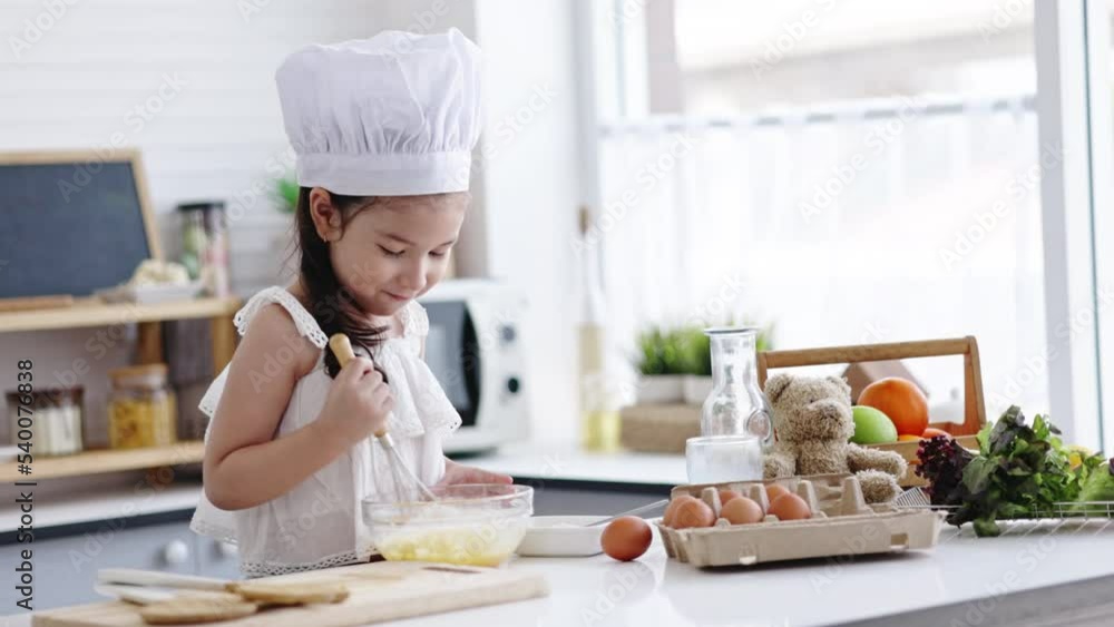 toddler girl is learning to cook bread in the kitchen with her mom with ...