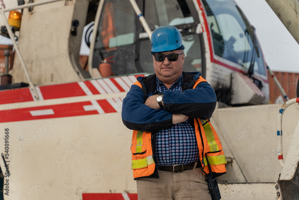 An employee in helmet and work uniform stands with his arms crossed in ...