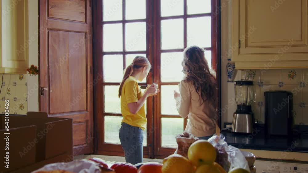 Blonde woman pointing at the window while showing something to her teen ...