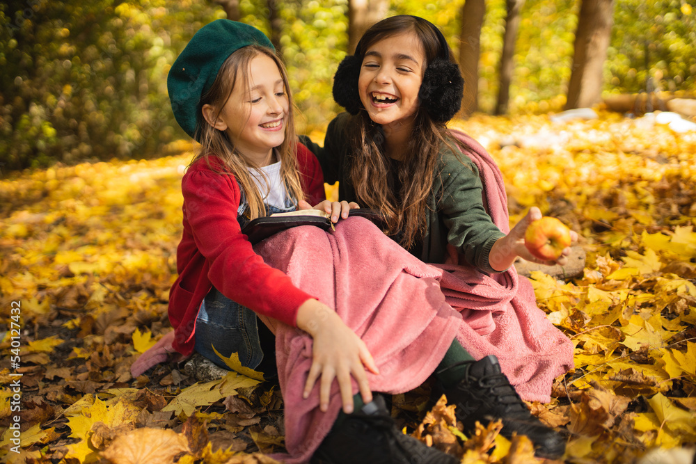 Two sisters in the forest covered with a blanket are sitting next to ...