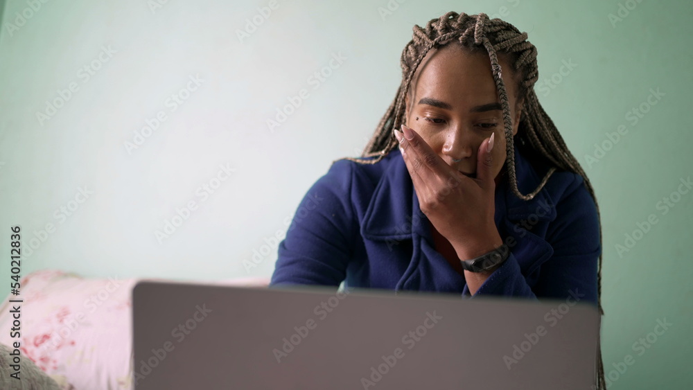One young black woman reacting with shock to notification on laptop ...