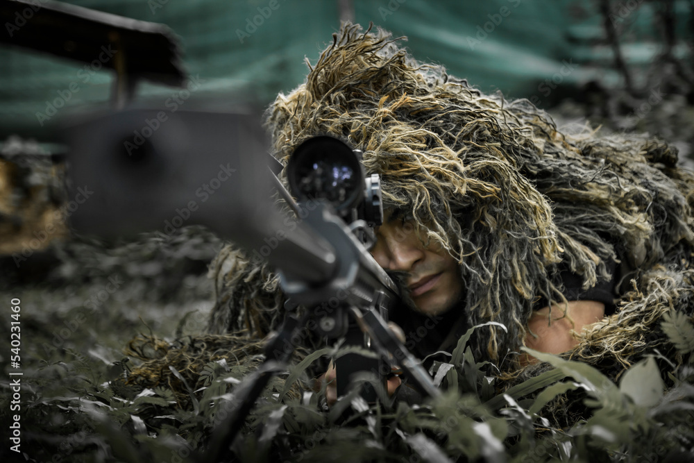 Man in a ghillie suit hidden in the forrest, aiming through a scope on ...