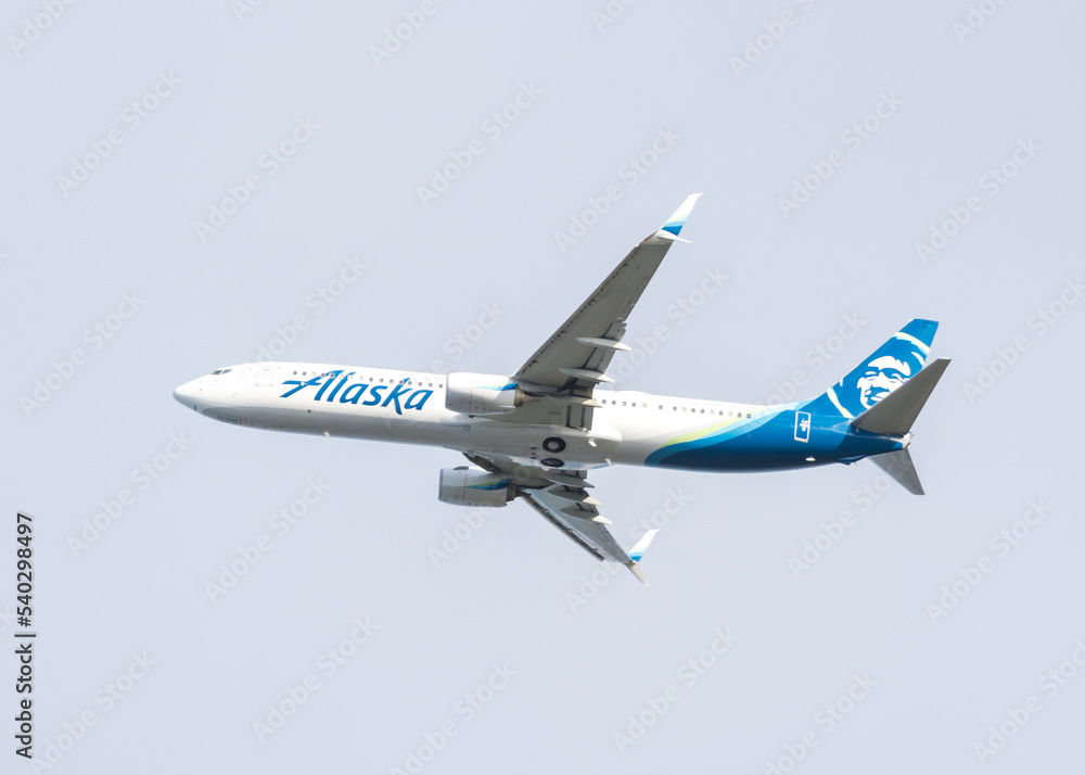 Flying airplane from Alaska Airlines isolated on blue sky background. A ...