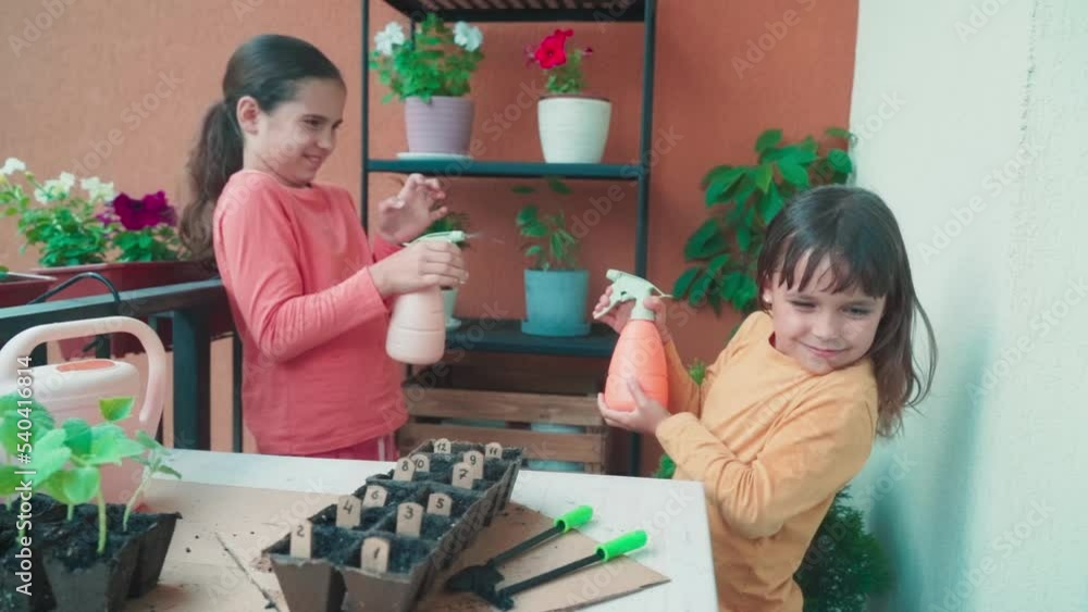 Happy sisters splash from spray guns on plants and around. Children ...