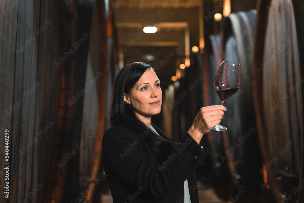 Woman in the wine cellar with barrels in background drinking and ...