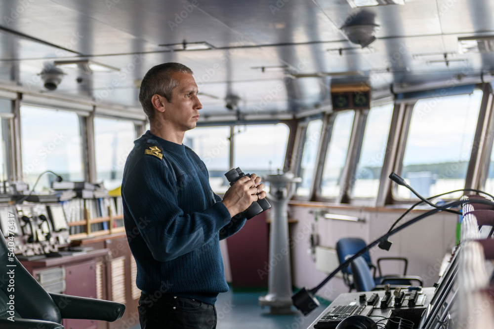 Deck officer with binoculars on navigational bridge. Seaman on board of ...