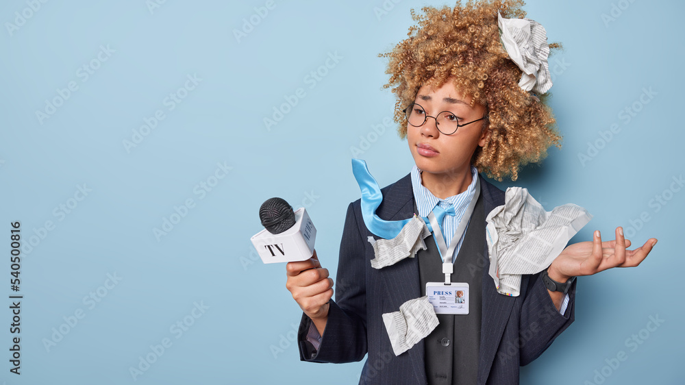 Professional female reporter feels confused shrugs shoulders stands ...