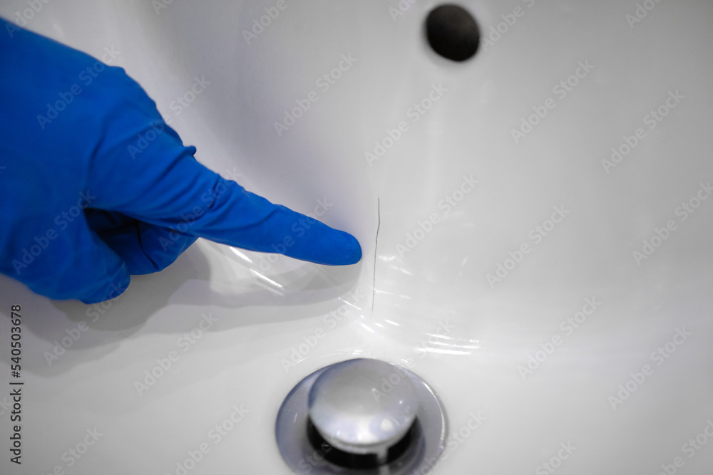 A gloved hand points to a crack in the sink. Factory defect on the ...