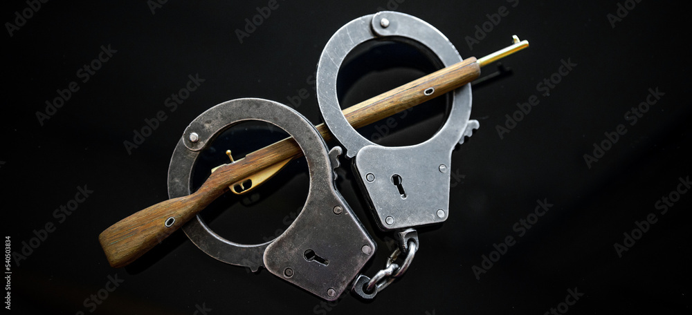Miniature wooden rifle in metal handcuffs on a black background. Arrest ...