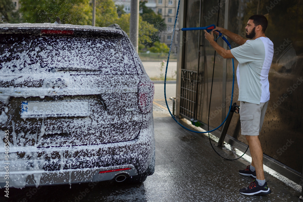 man washing a car in a self-service car wash station with wahing foam ...
