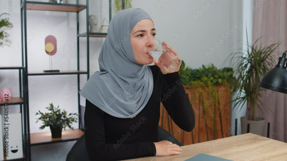 Thirsty young muslim woman in hijab holding glass of natural aqua make ...