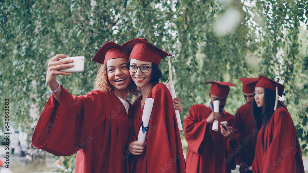 Pretty female graduates are taking selfie with diploma scroll using ...