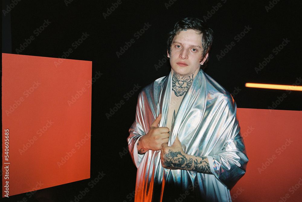 Portrait of young guy with tattoo in silk mantle looking at camera ...