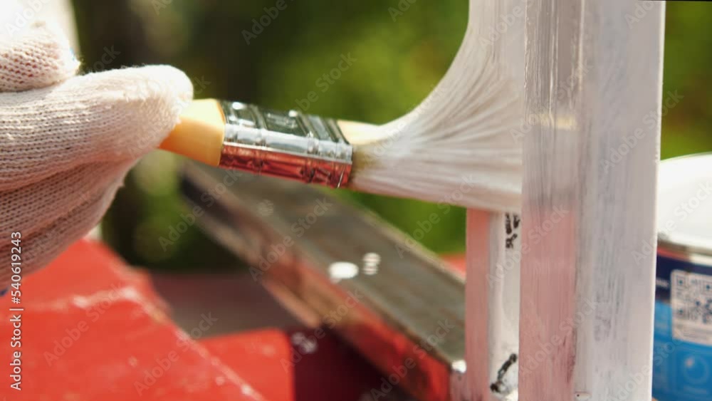 A hand in a rag glove is painting a metal profile with white paint ...