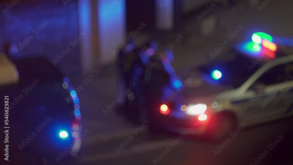 Group of police officers around blinking cop car, beacon light, blurry ...