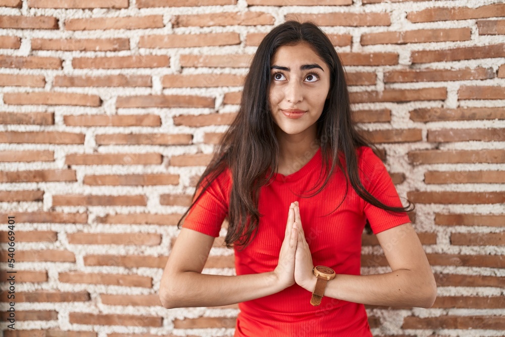 Young teenager girl standing over bricks wall begging and praying with ...