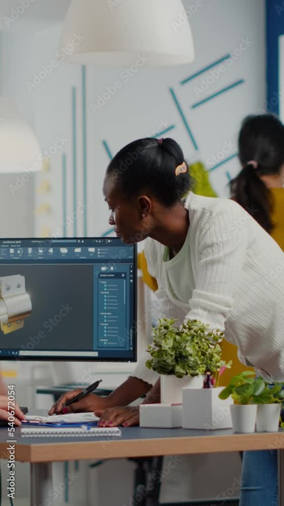 Diverse team of engineers working on computer at mechanical piece ...
