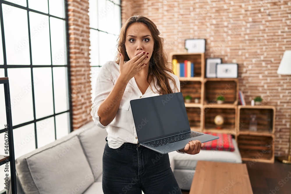 Young hispanic woman using laptop showing blank screen at home covering ...
