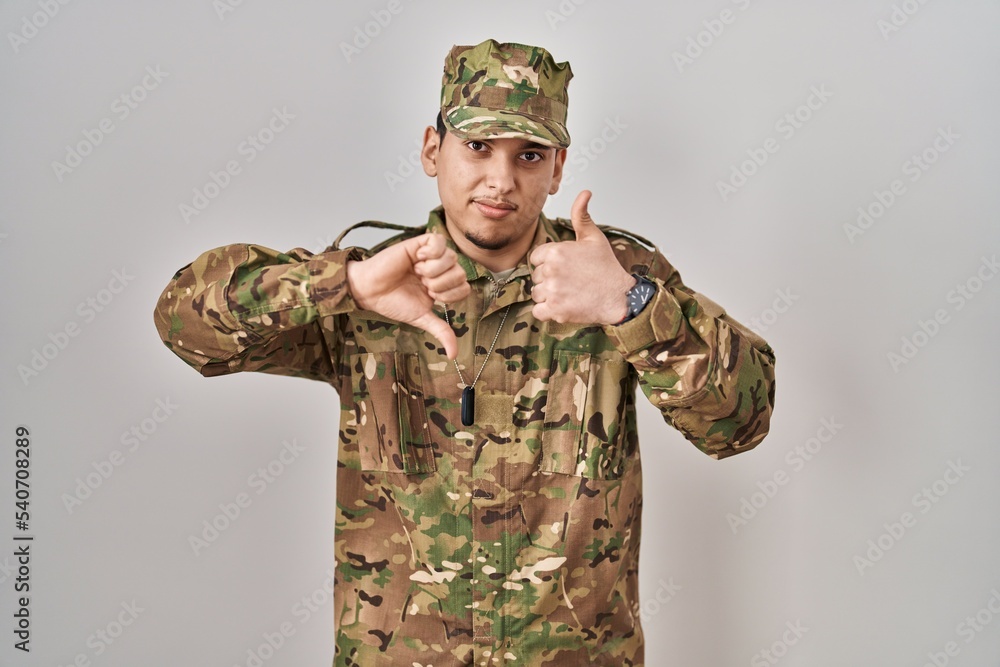 Young arab man wearing camouflage army uniform doing thumbs up and down ...