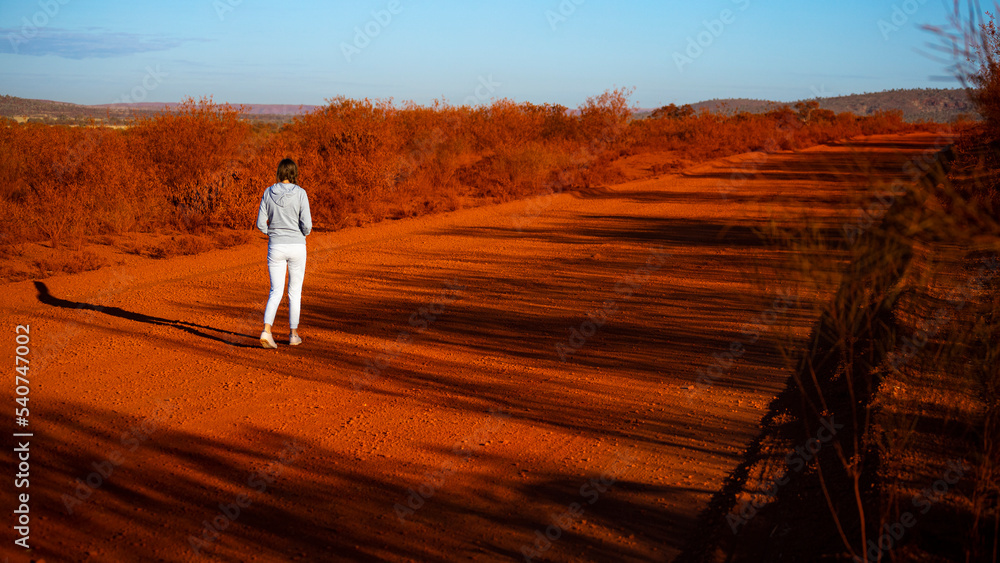 girl walks along red dirt road in karijini national park in western ...