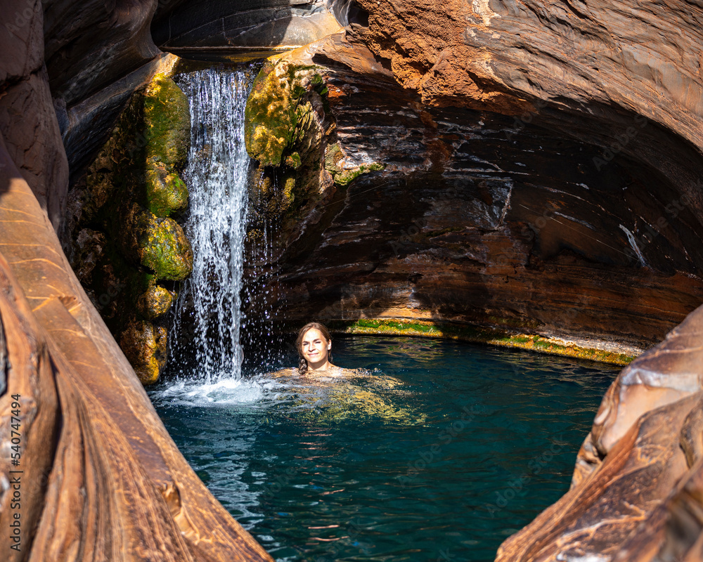 A girl in a white bikini relaxes in a rock pool with a waterfall ...