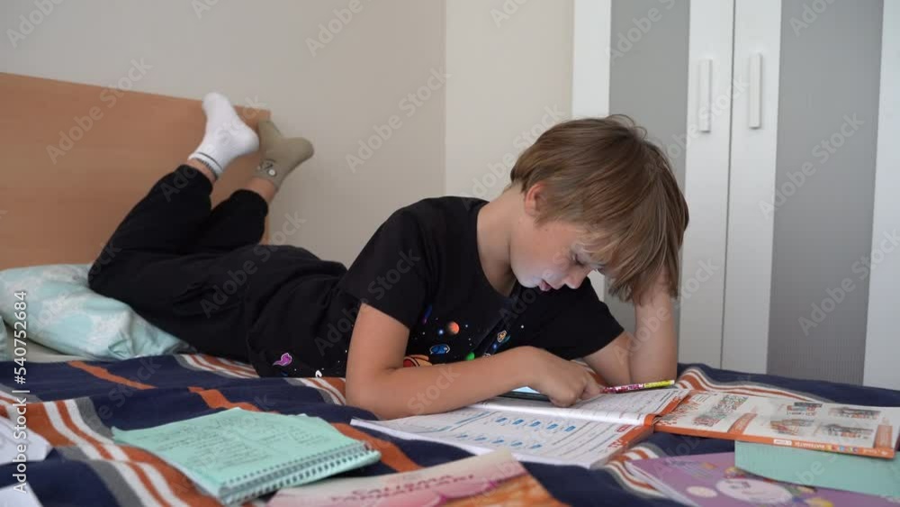 Preteen child doing homework exercise lying on bed at home. Using ...