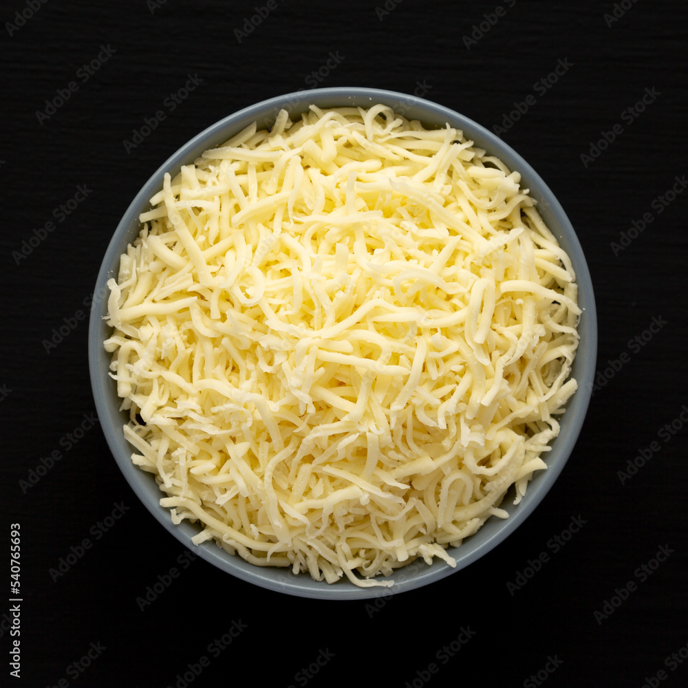 Shredded Mozzarella Cheese in a Bowl on a black surface, top view. Flat ...