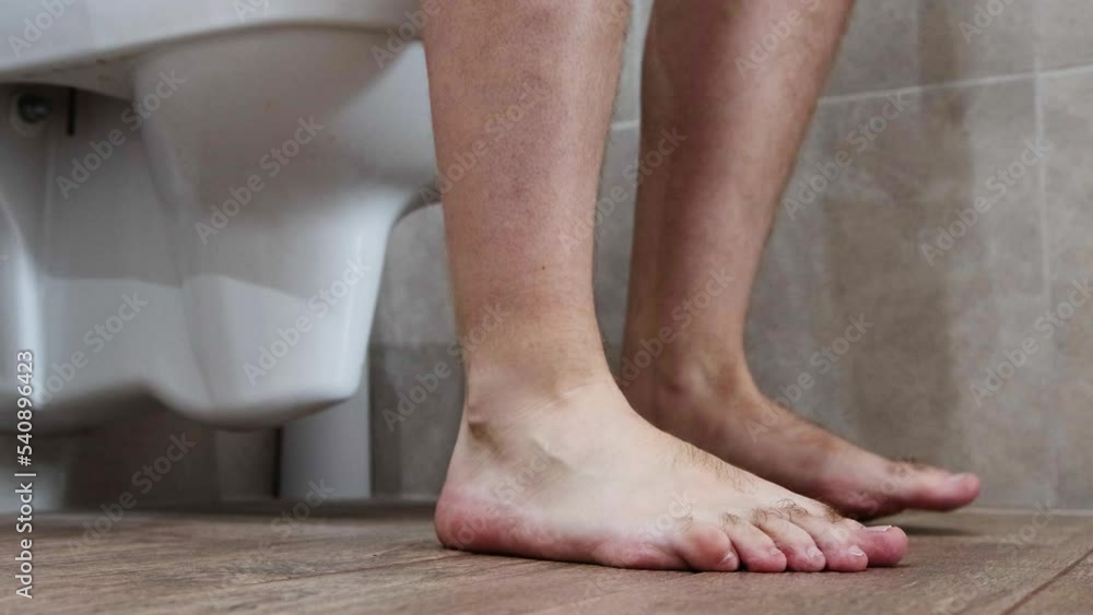 A man goes to the toilet in the toilet, takes off his denim shorts and ...