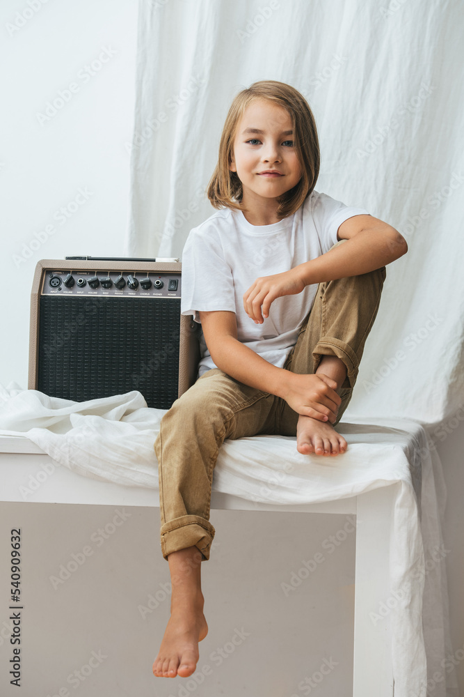 Cute tween girl sitting on a table barefoot next to a guitar amp. Stock ...