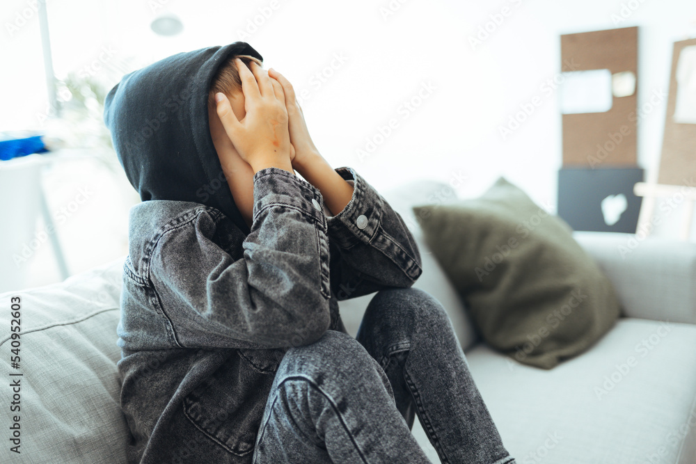 Little boy suffering from child abuse curled up on the sofa. Depressed ...