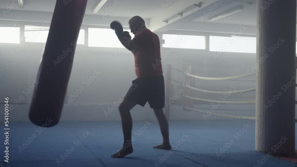 Mid adult fighter training hand and leg punches with boxing pear in ...