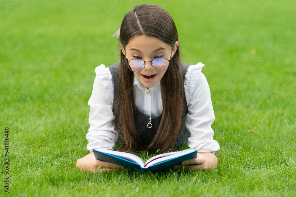 Portrait of surprised girl reading book lying on grass, reading. Teen ...