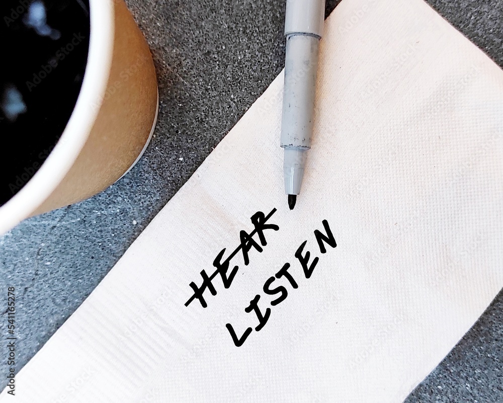 Paper coffee napkin with handwritten text HEAR changed to LISTEN, means ...