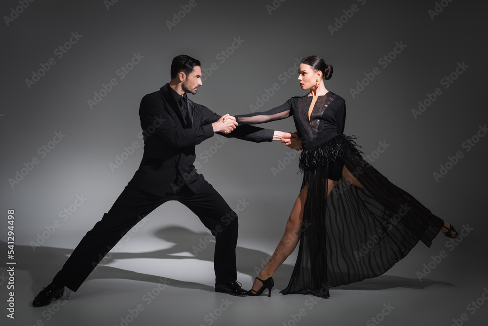 Side view of elegant couple performing tango on grey background with ...