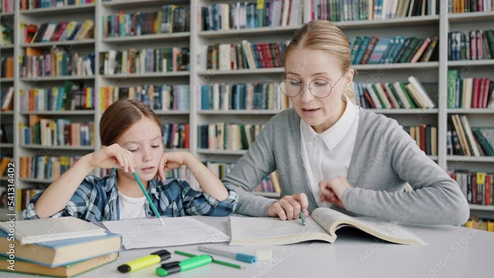 Experienced teacher helps pupil do homework in library Stock Video ...