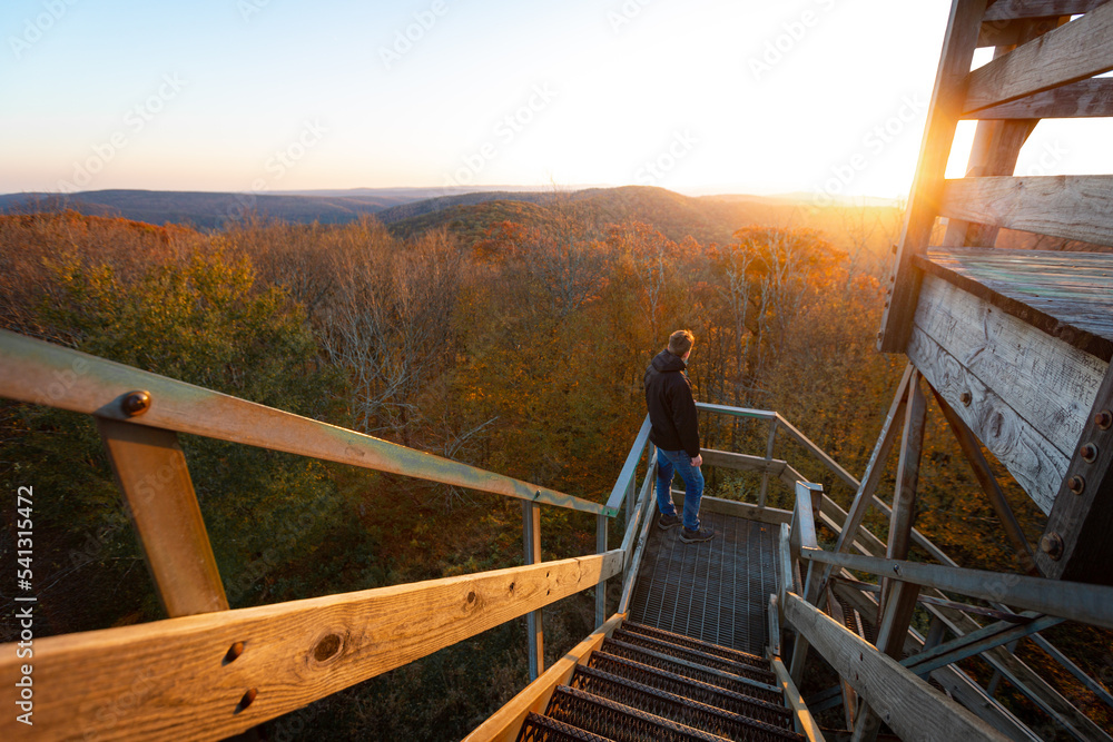 Adventurous young man soaks in the sunrise on stairs of wooden ...